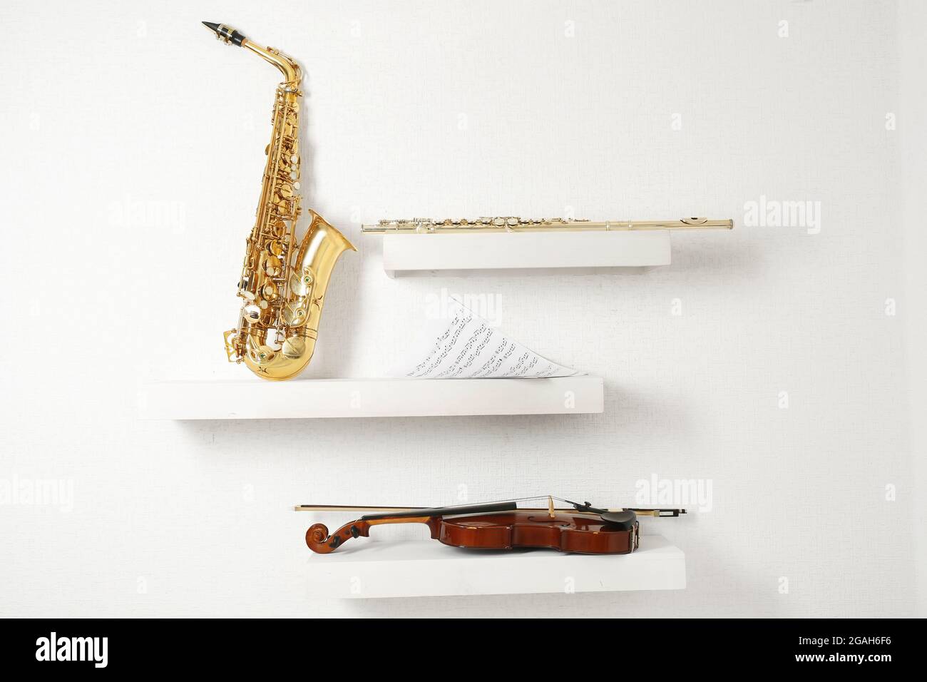 Violin, flute and saxophone on decorated shelves against white wall ...