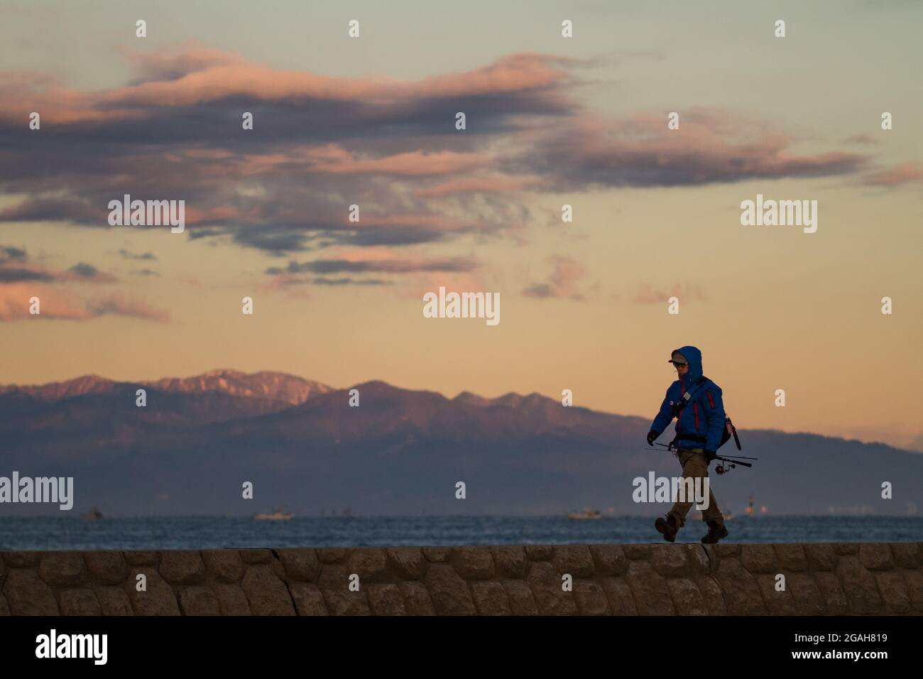 An angler walking on the harbour wall in Muira early in the morning ...
