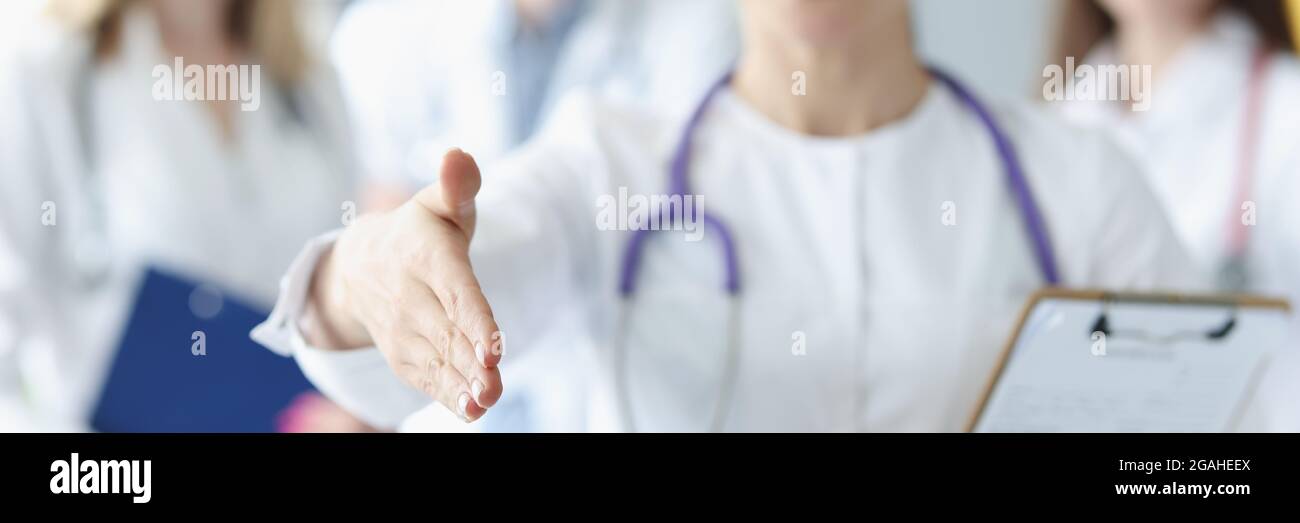 Woman doctor stretches out her hand for greetings against background of ...