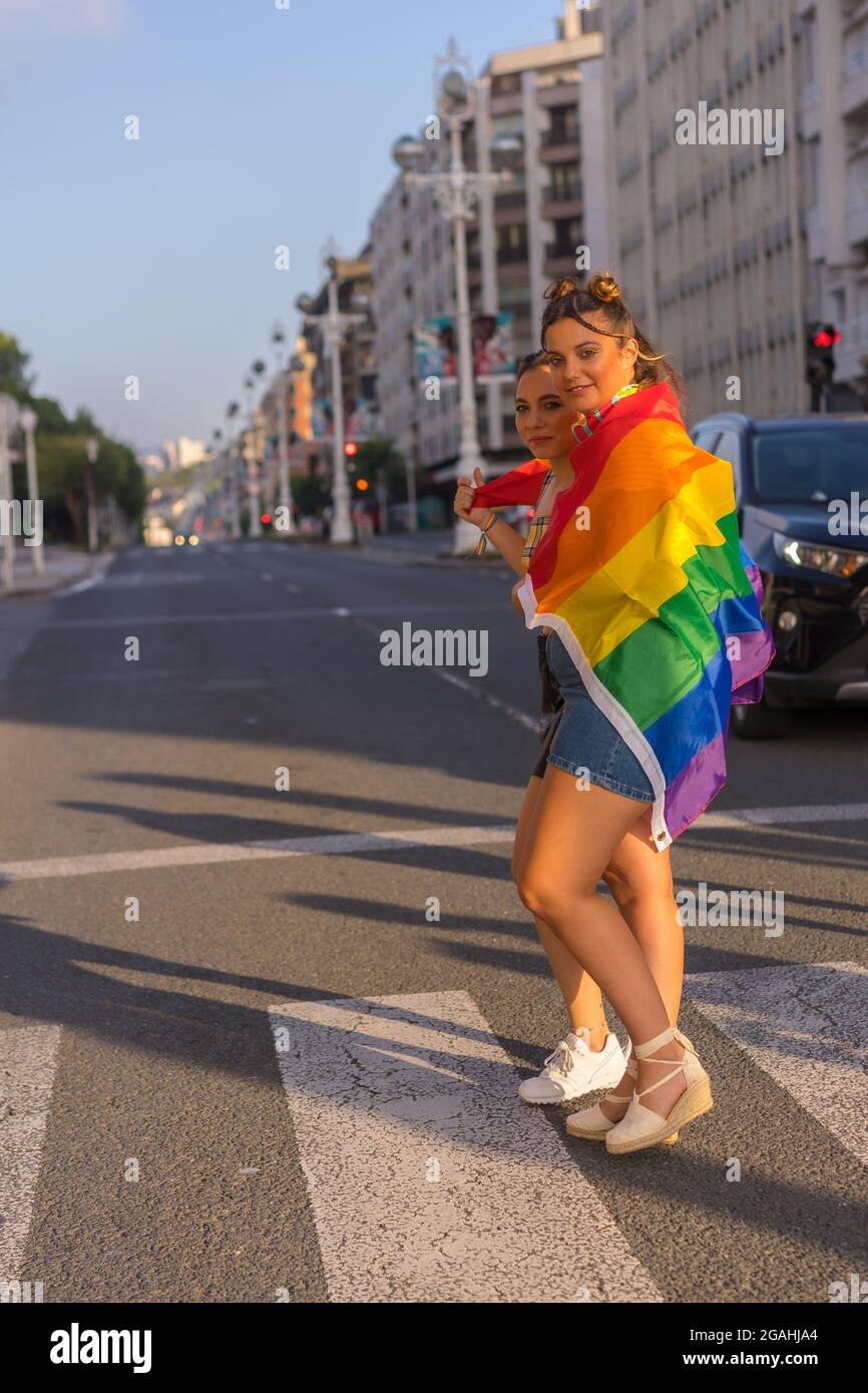 Vertical shot of two young Caucasian hugging females passing street ...