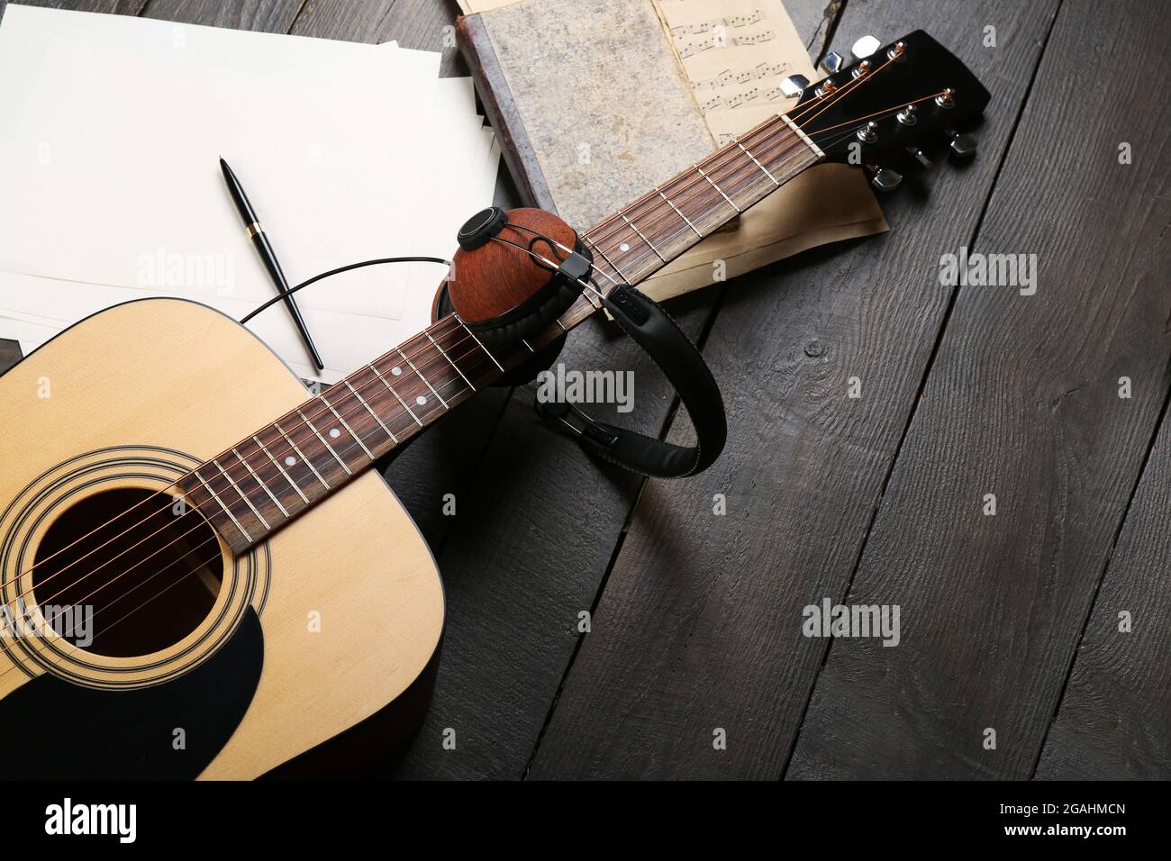 Acoustic guitar, headphones, musical notes and white papers on wooden ...