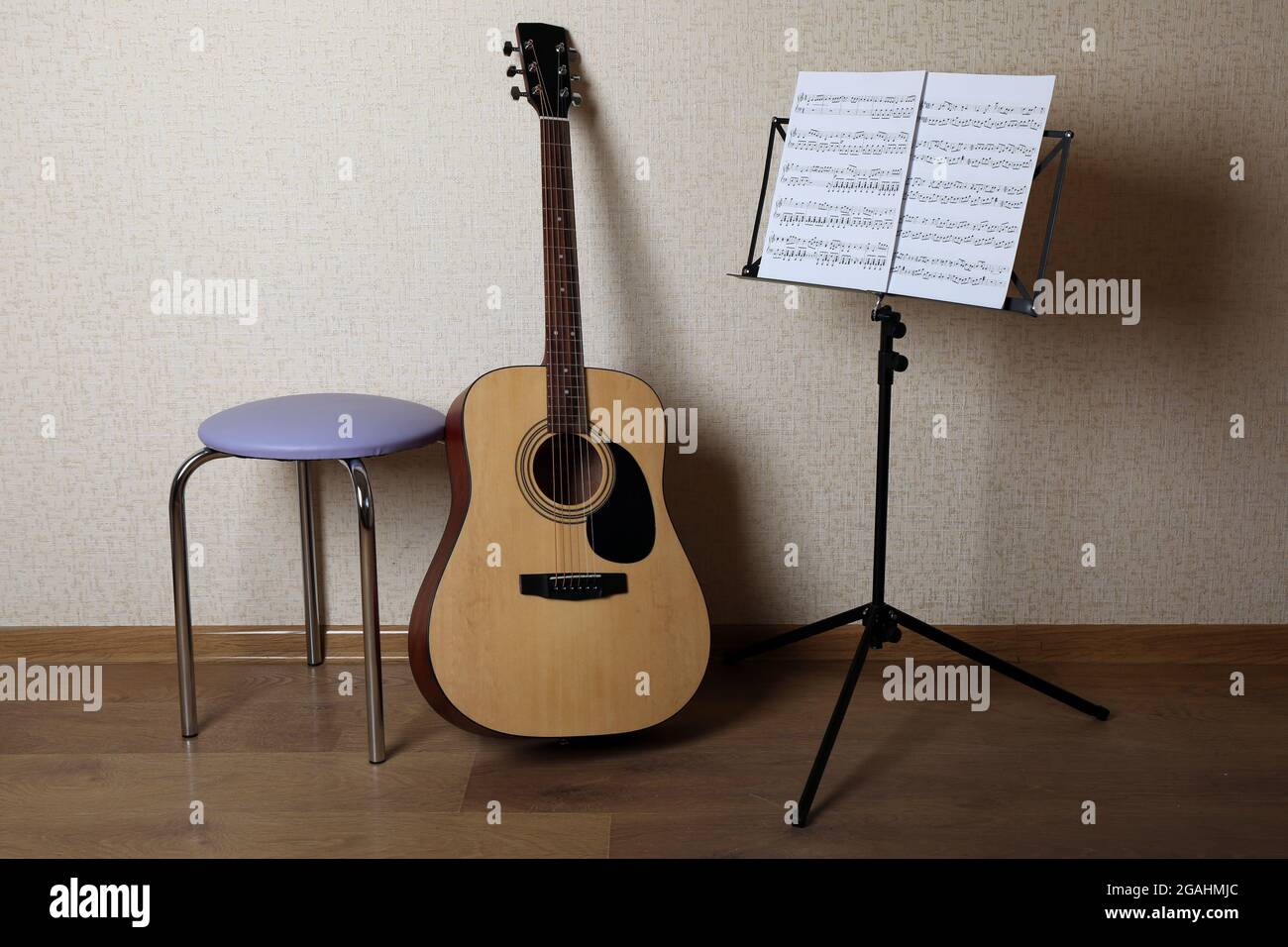 Acoustic guitar propped on wall with stool and musical notes holder in ...