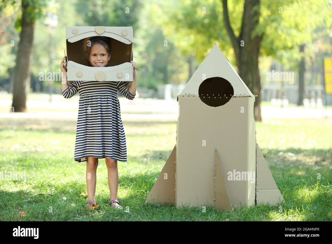 Pretty little girl in box helmet standing near carton rocket in the ...
