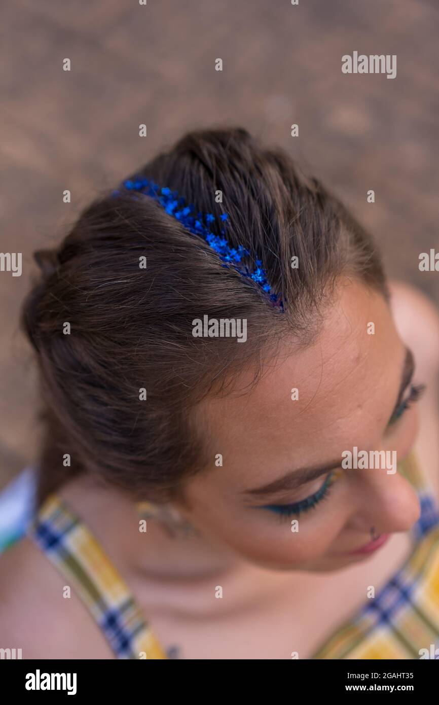 Vertical shot of a Caucasian young female with blue tinsel in her hair ...