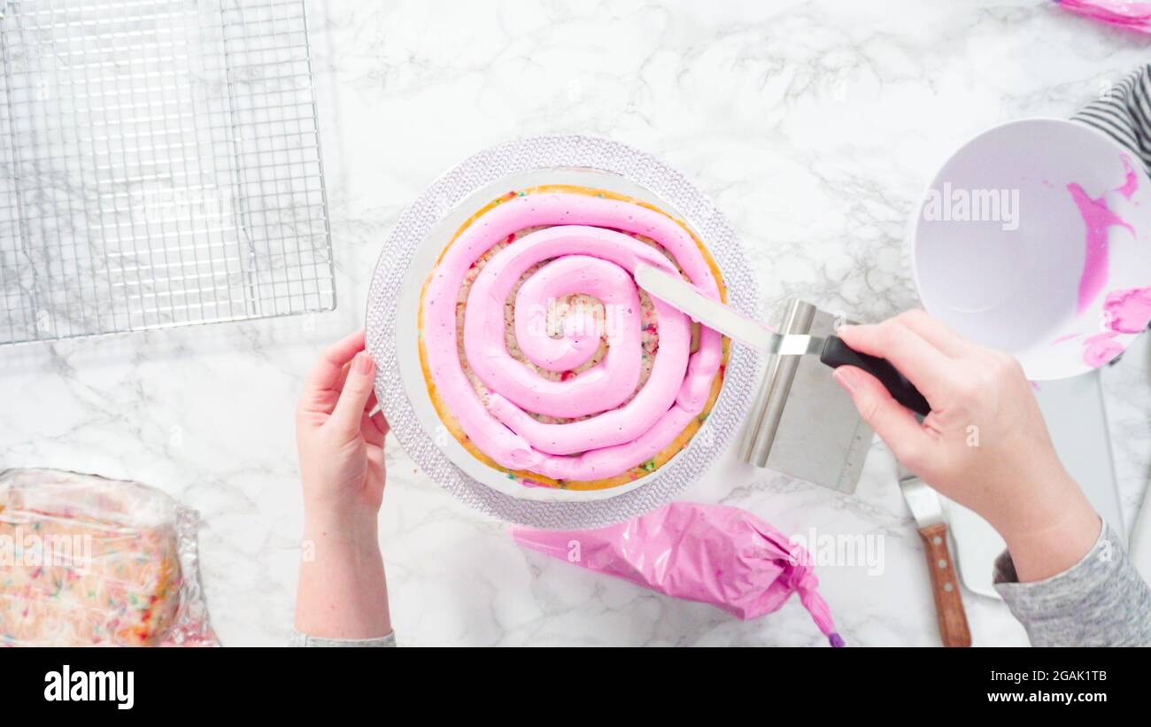 Flat lay. Step by step. Frosting round funfetti cake layers with pink ...