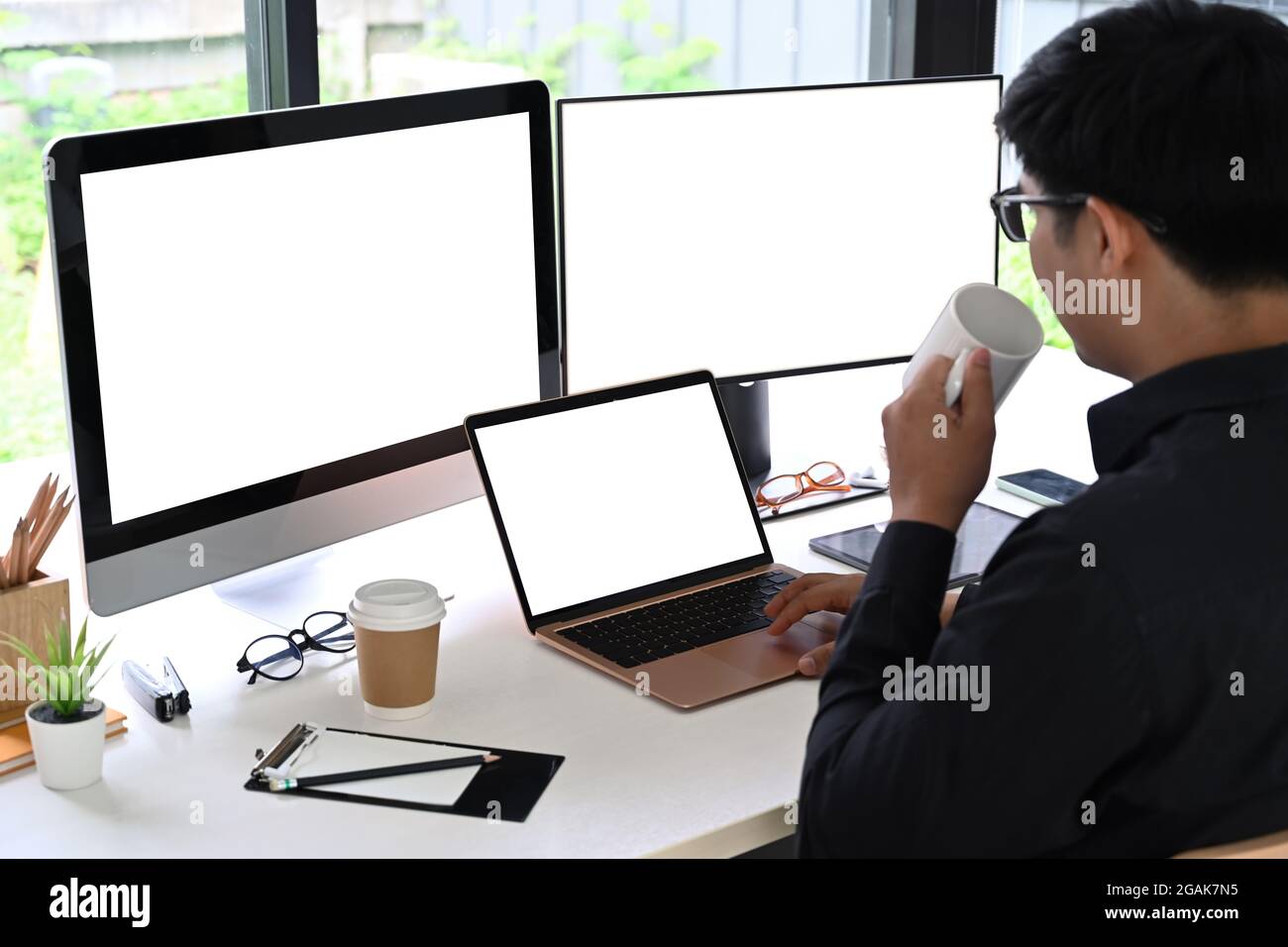 Back view man programer drinking coffee and working in modern workplace ...