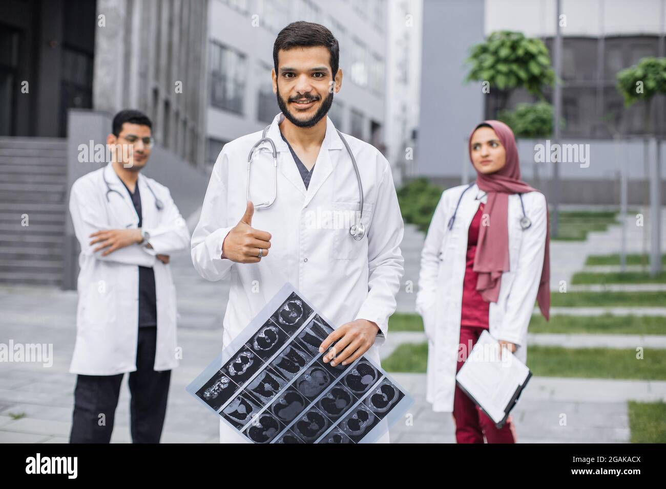 Confident team of multiracial three doctors in scrubs and coats ...