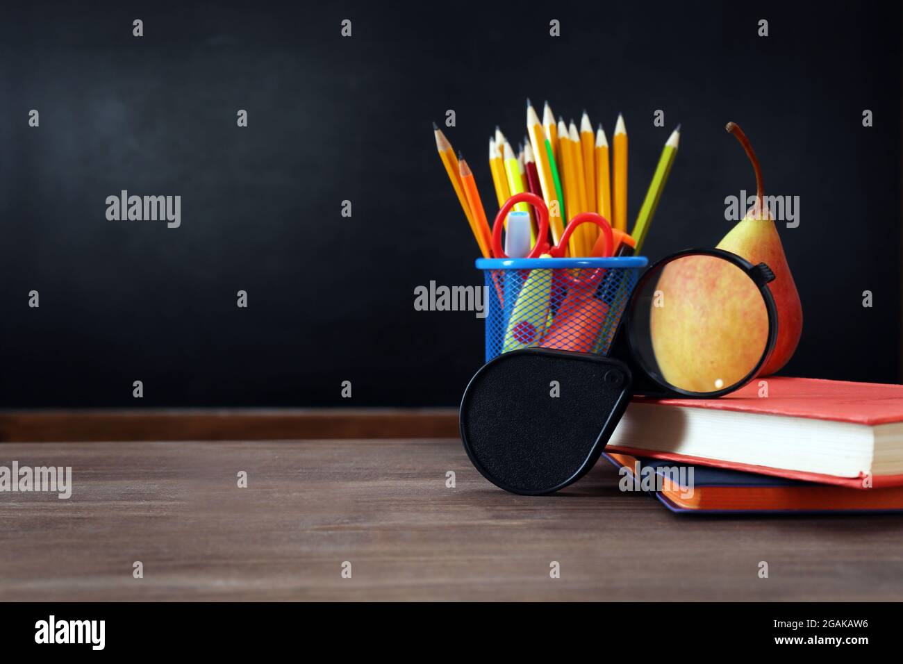 Pear, magnifier and clock with books on desk background Stock Photo - Alamy