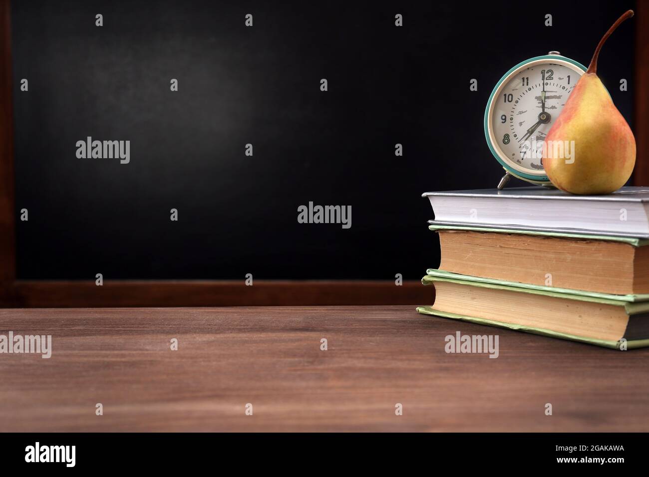Pear and clock with books on desk background Stock Photo - Alamy
