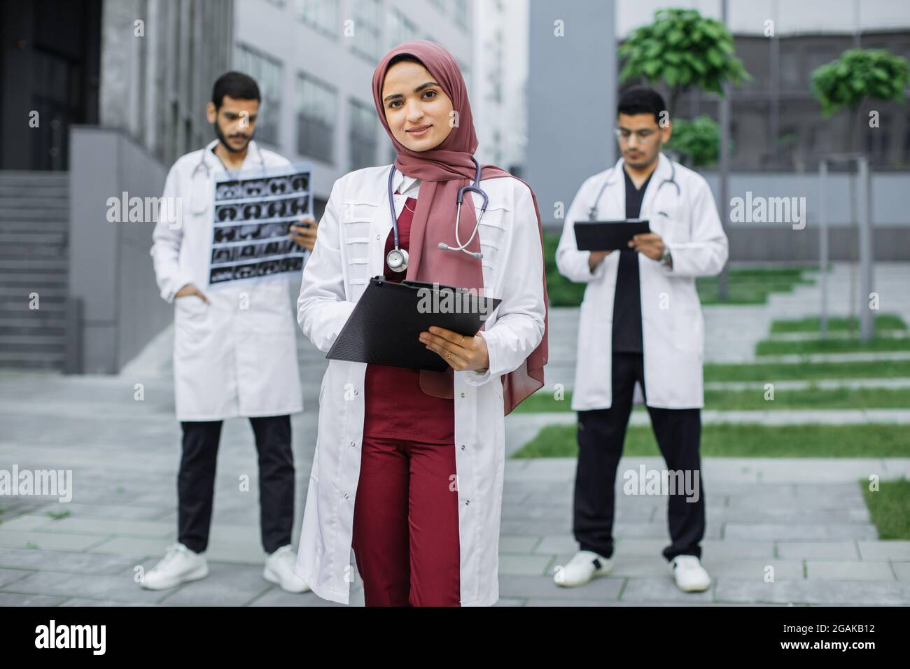 Female Muslim pleasant doctor in hijab, standing with clipboard ...
