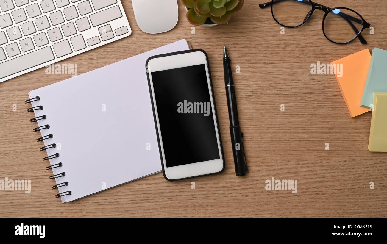 Mock up mobile phone, notebook, sticky notes and glasses on wooden desk ...
