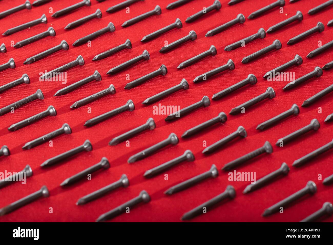 lot of black steel nails, on red background, arranged diagonally ...