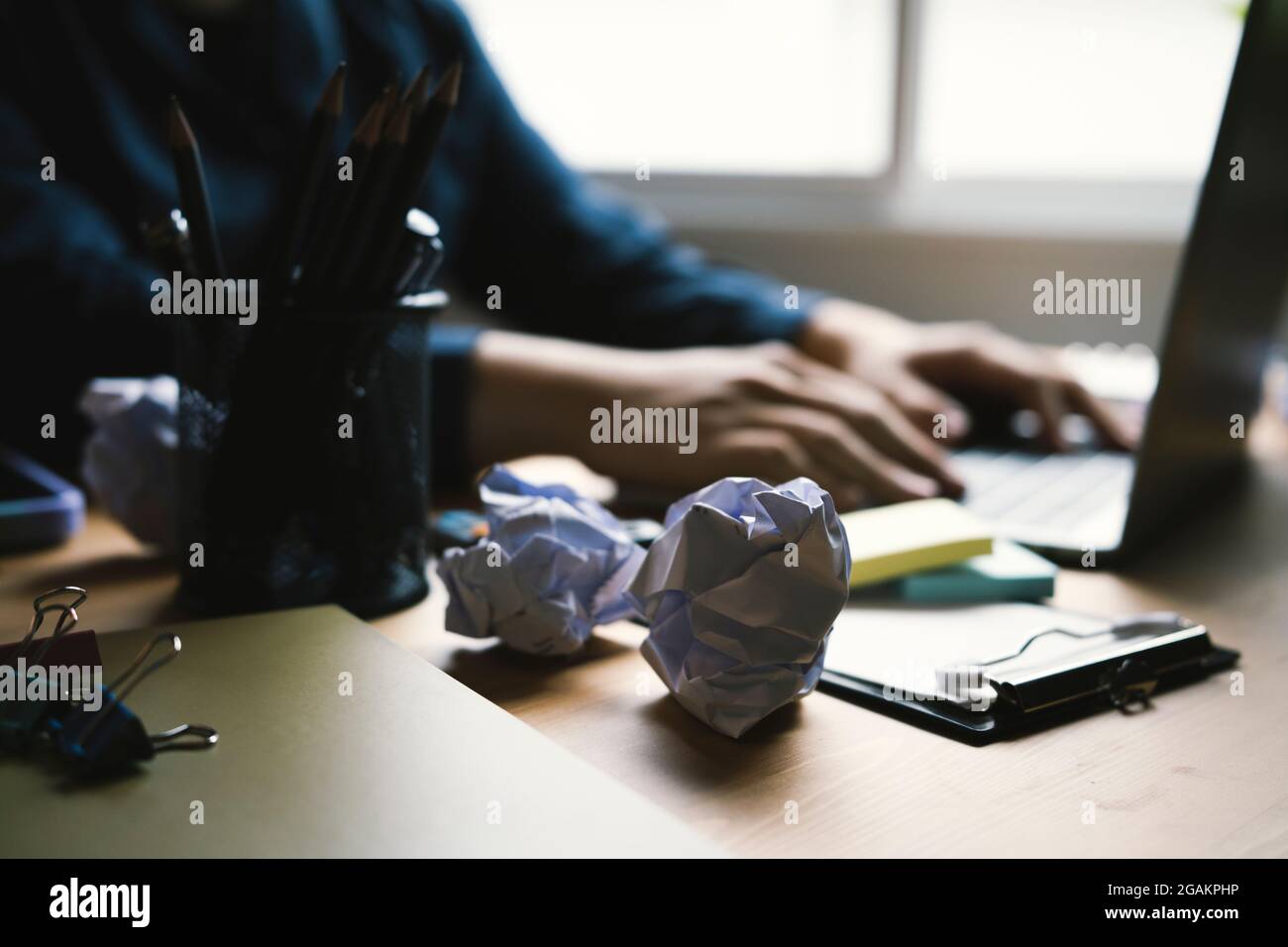Crumpled paper on office desk with businessman working with laptop in ...