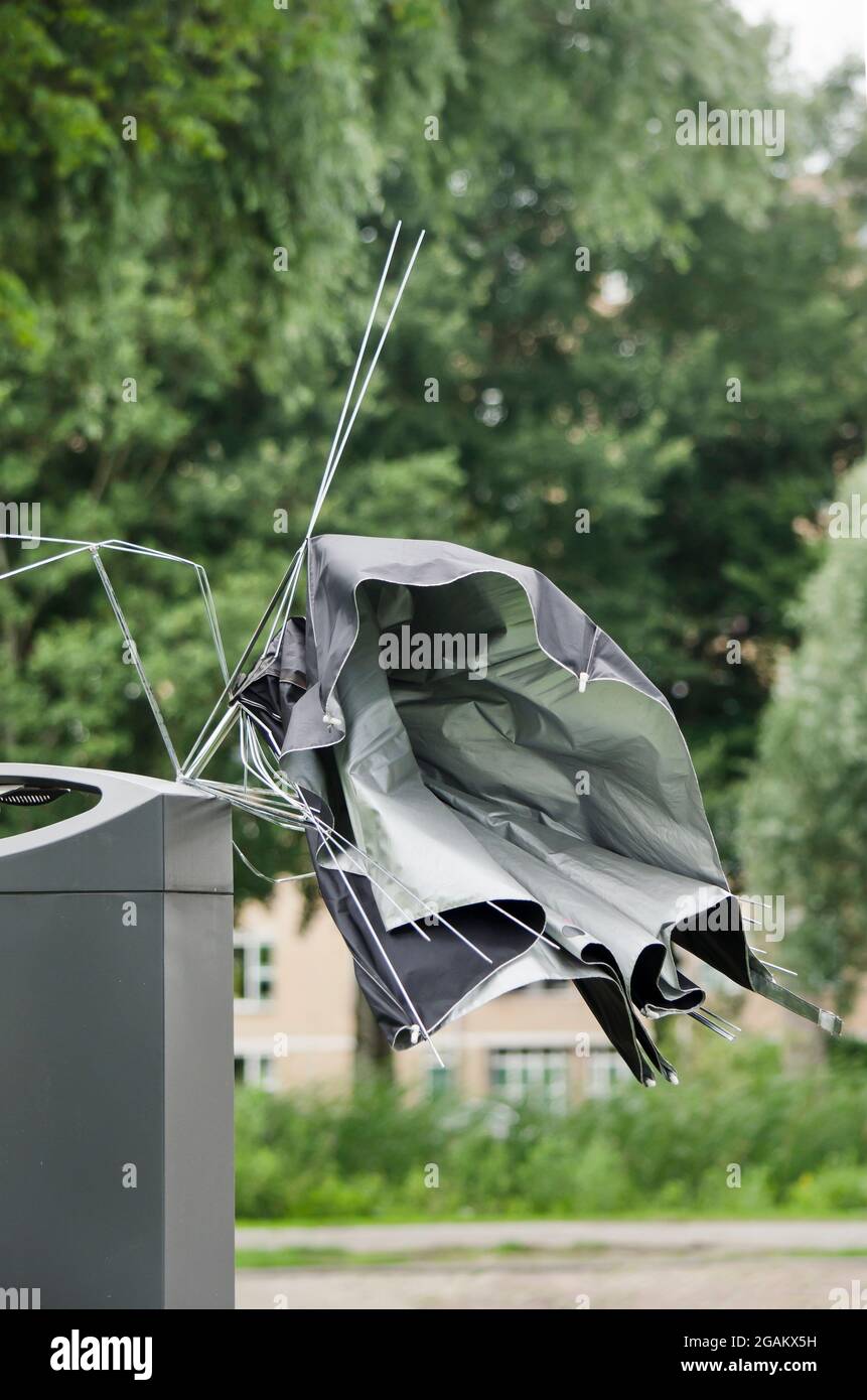 Severely damaged black umbrella sticking out of an urban trash can on a ...