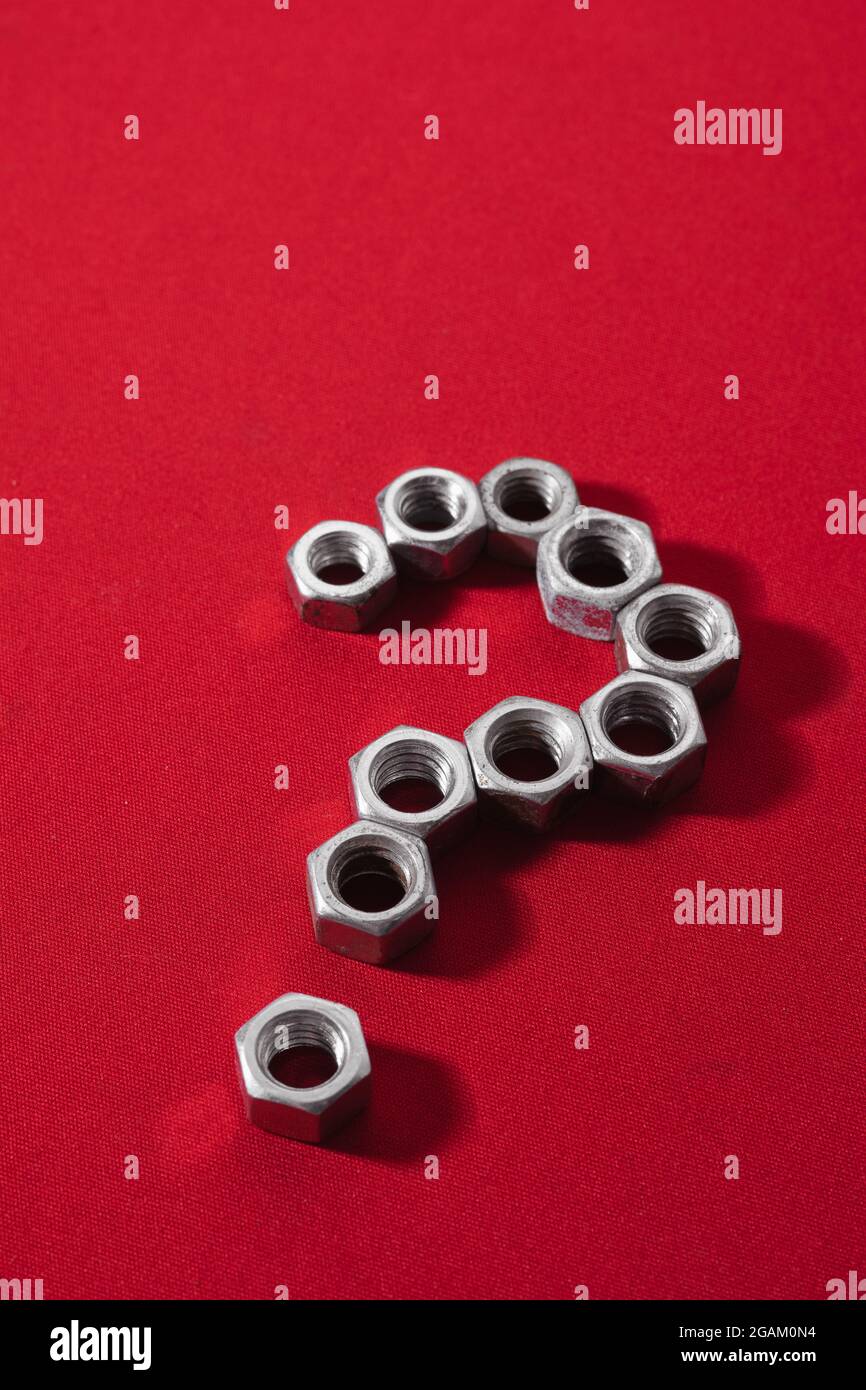 Question mark, made with steel nuts on red cloth background, leaving ...