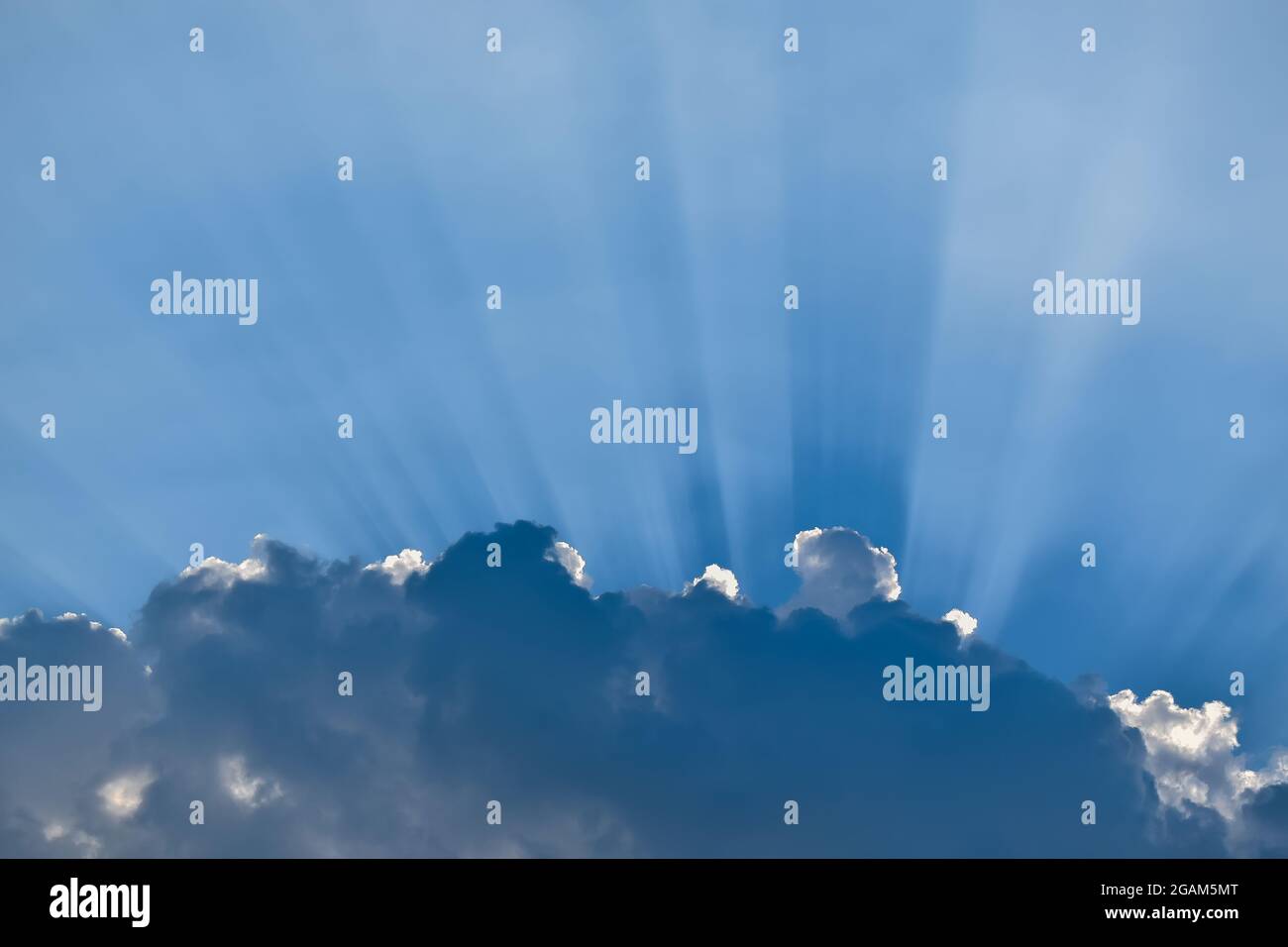 Sun behind the clouds with sun rays streaks in the cloudy blue sky with ...
