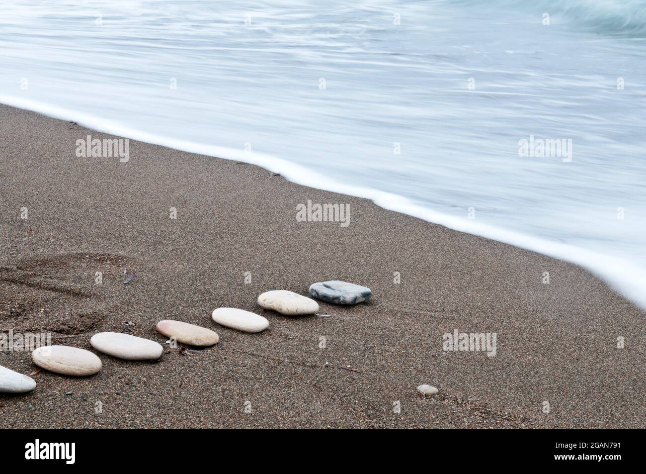 Smooth beach stones in a raw on a sandy coastline and foam of sea water ...