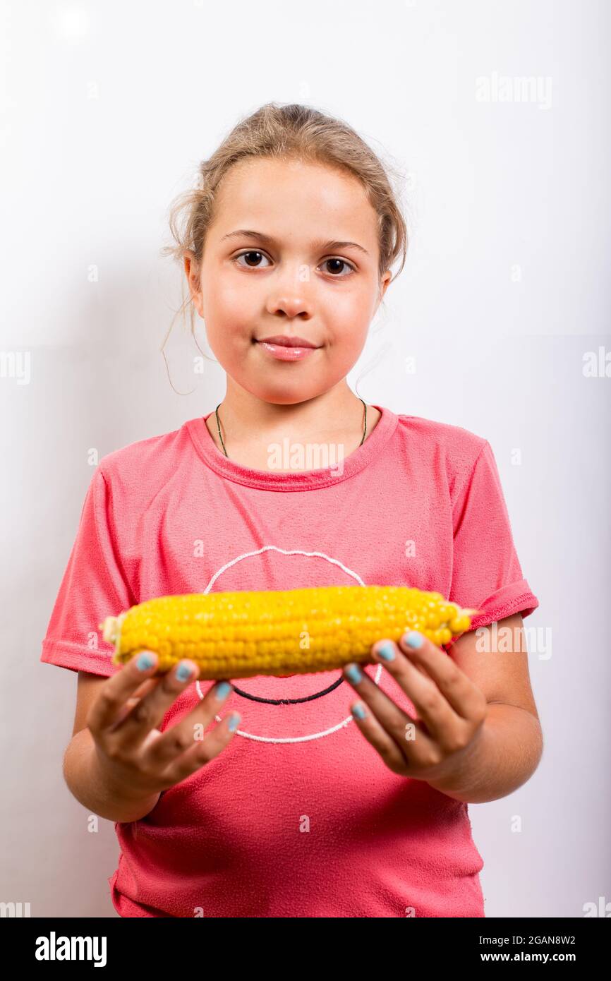 A tanned school-age girl holding a swing of corn on a white background ...