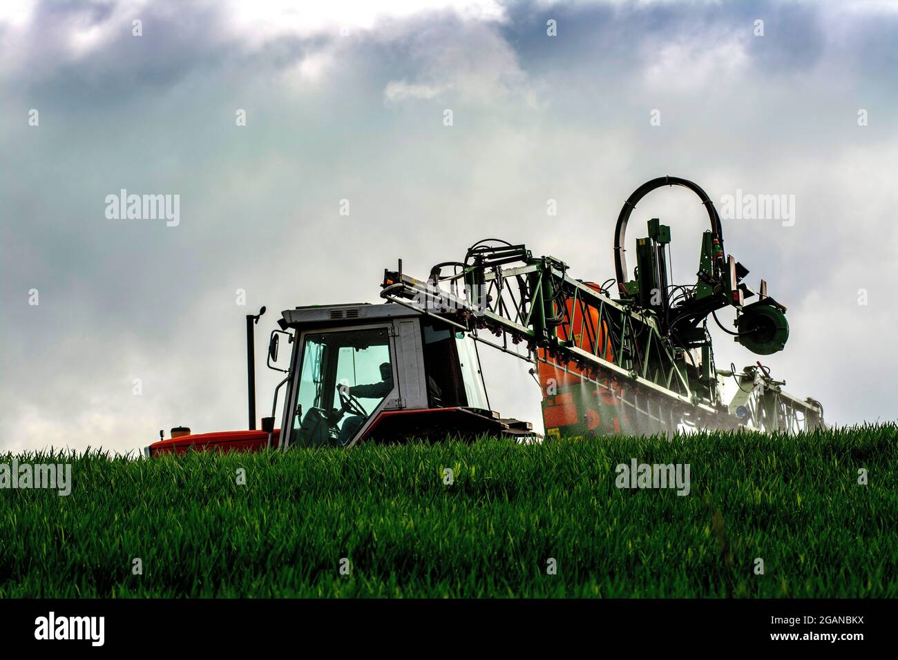 Tractor spraying crops in a lush field under dramatic skies during ...