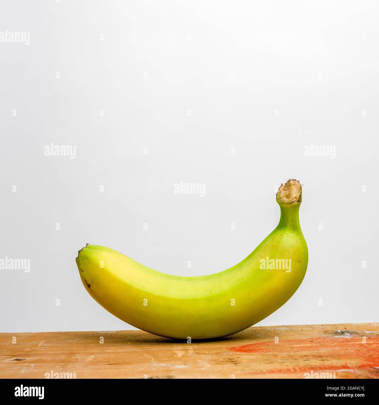 Fresh green banana resting on a wooden surface with a neutral ...