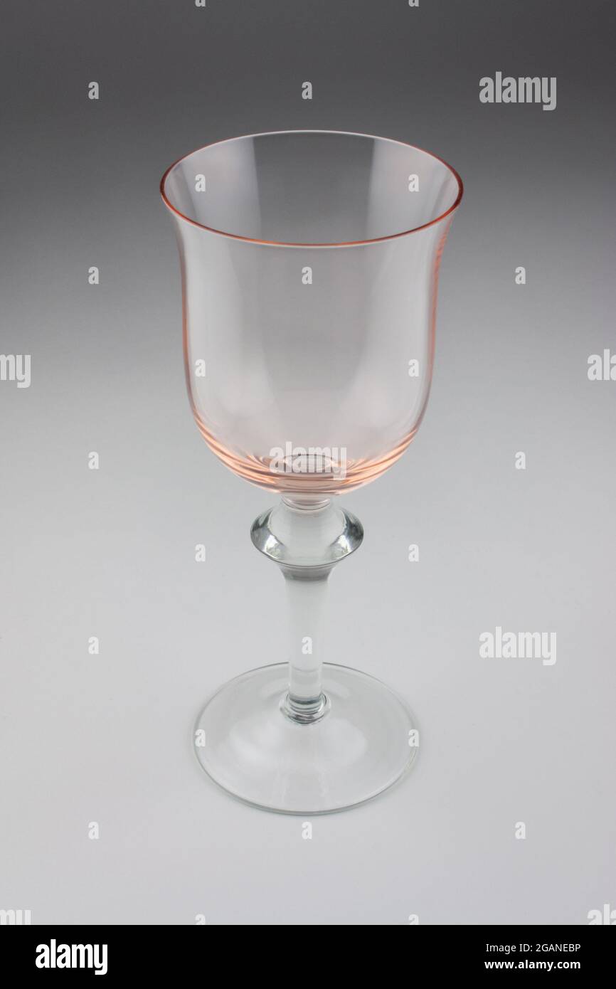 a single, empty wine glass made of pink tinted glass on a soft gray ...