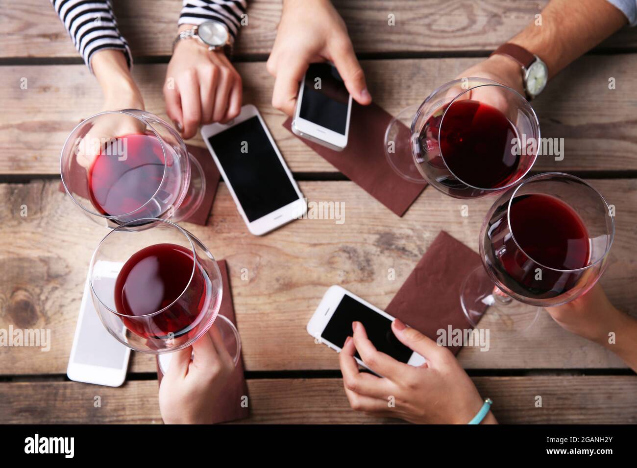 Four hands with smart phones holding glasses with red wine, on wooden ...
