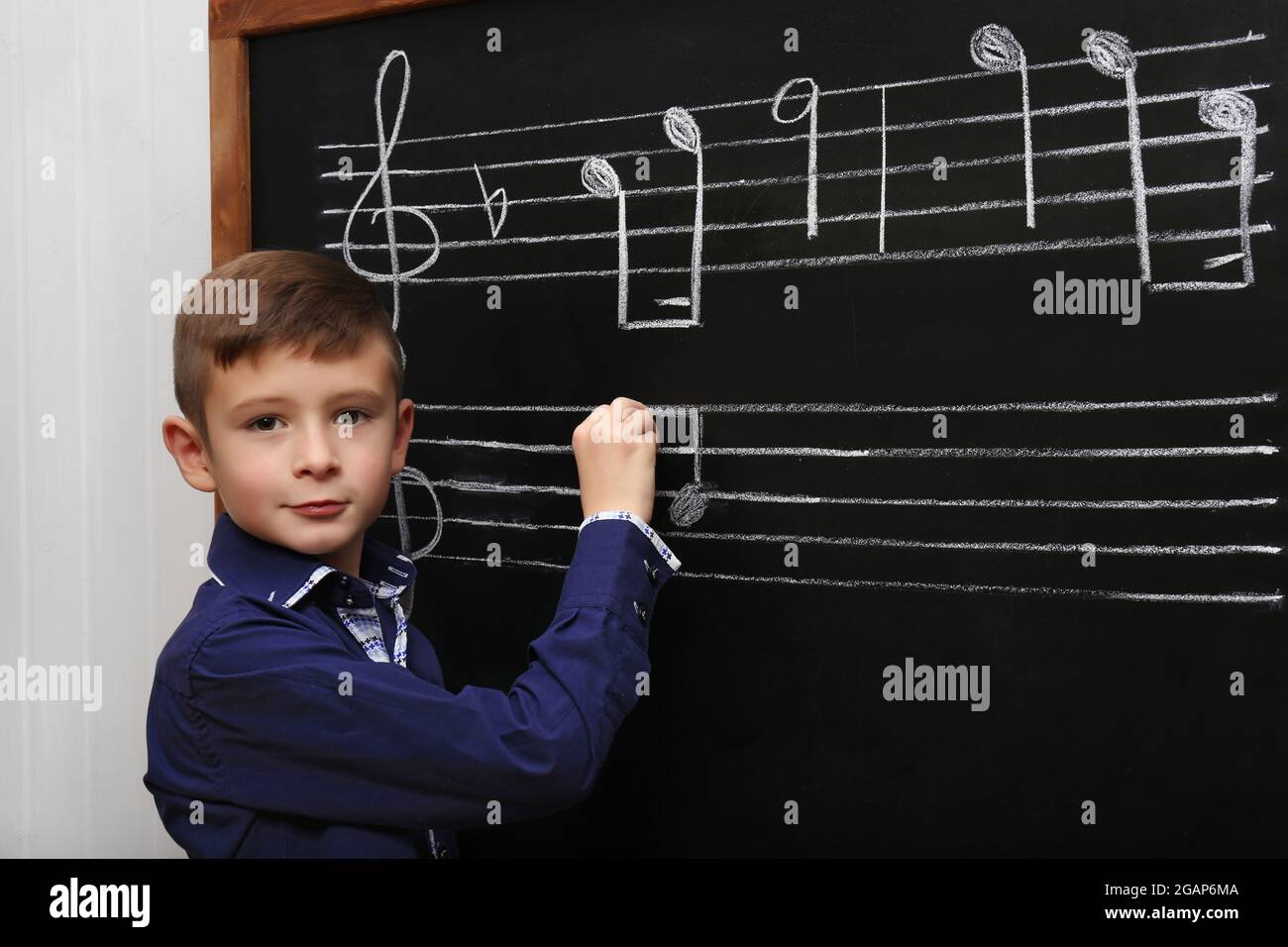 Cute boy writing at the blackboard with musical notes, in the classroom ...