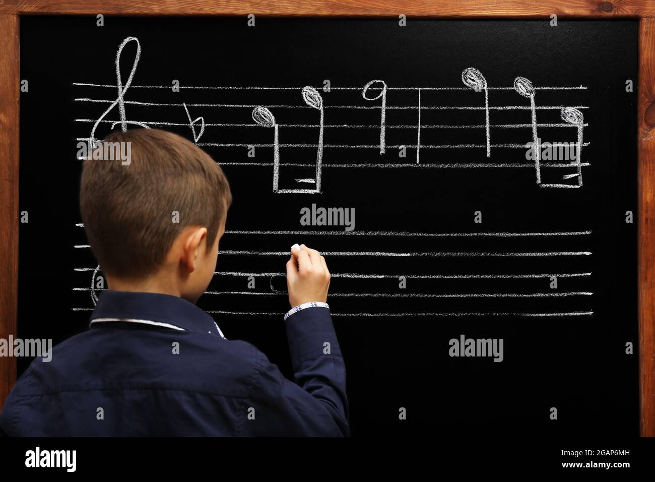Cute boy writing at the blackboard with musical notes, in the classroom ...