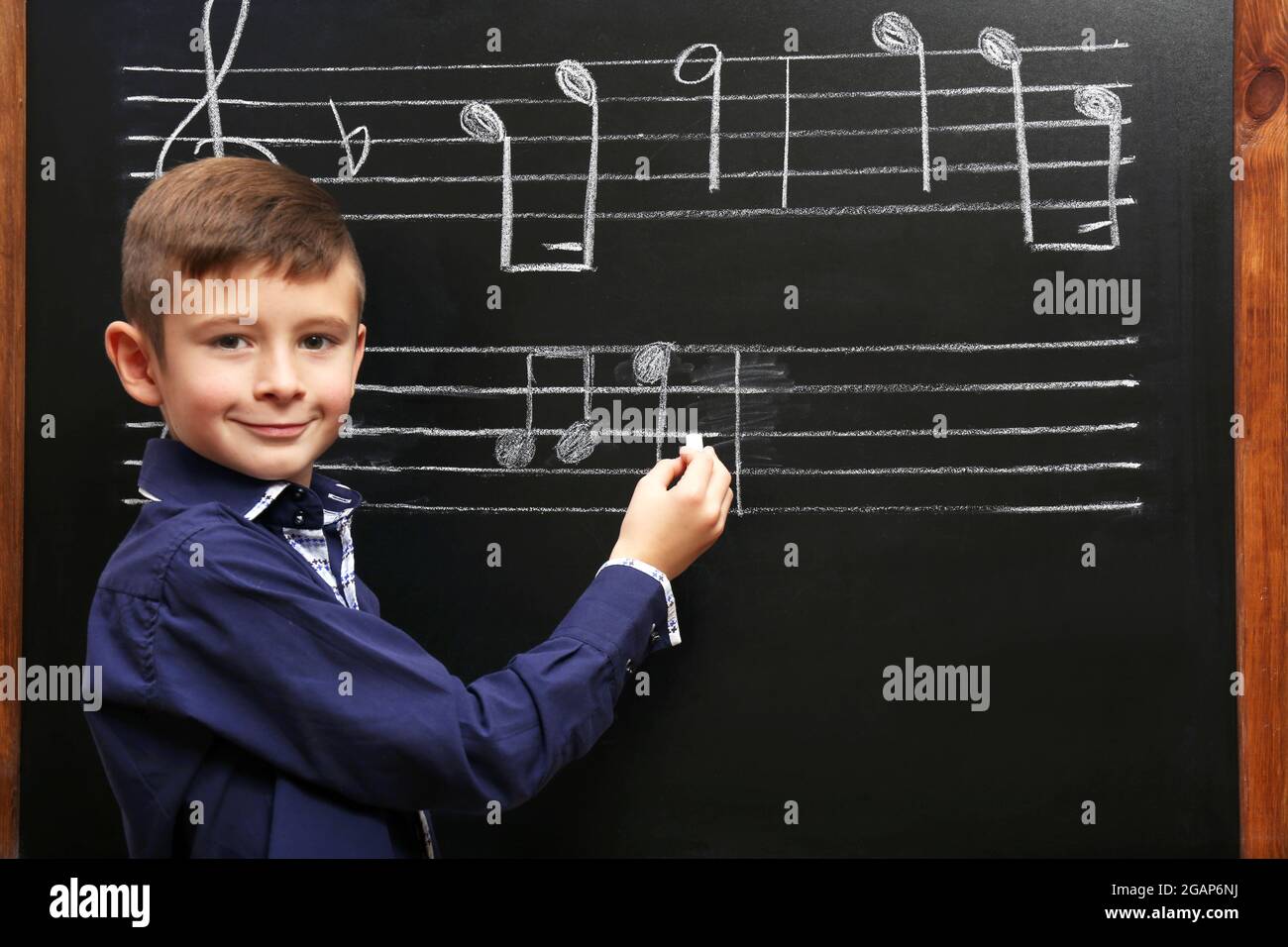 Cute boy writing at the blackboard with musical notes, in the classroom ...