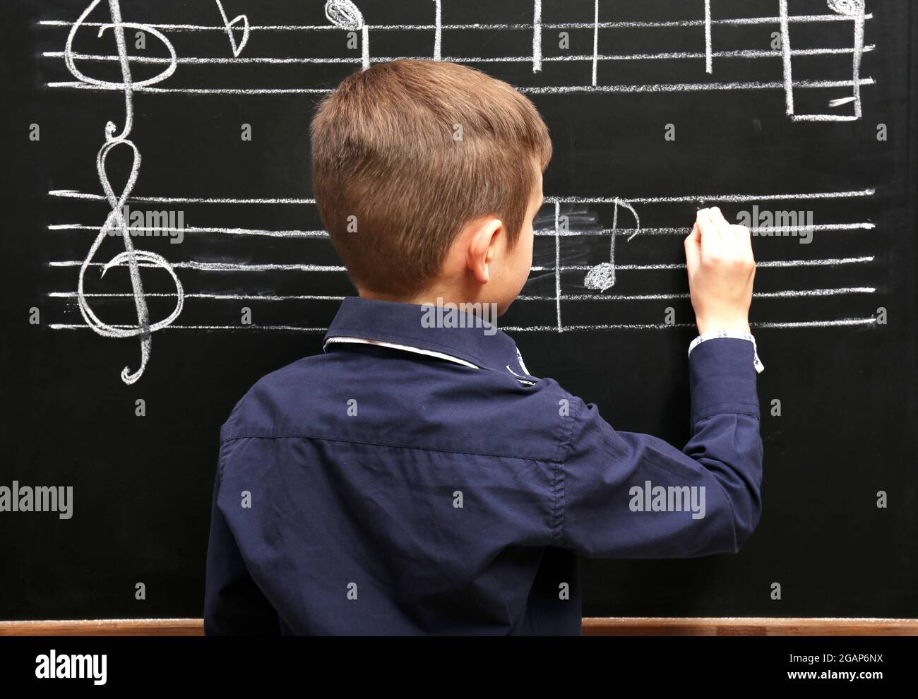 Cute boy writing at the blackboard with musical notes, in the classroom ...