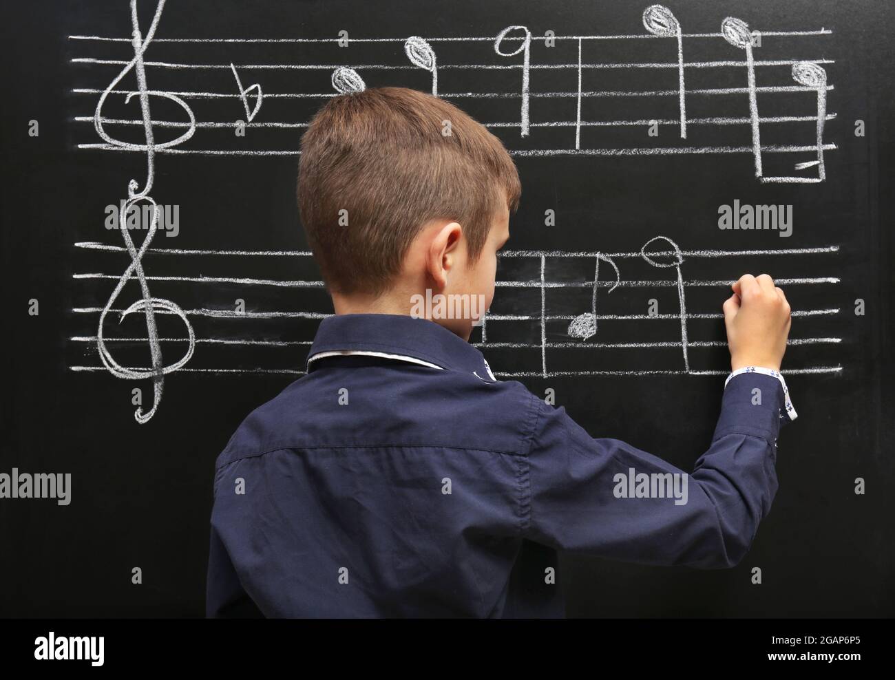 Cute boy writing at the blackboard with musical notes, in the classroom ...