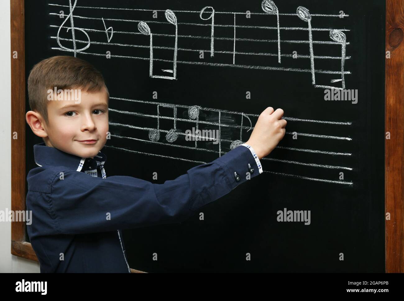 Cute boy writing at the blackboard with musical notes, in the classroom ...