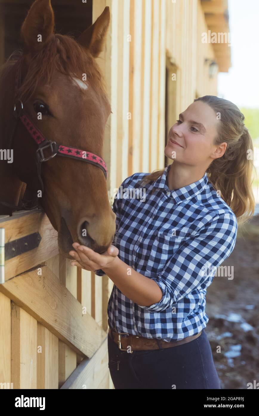 Female horse owner standing at the horse stable embracing a dark bay ...