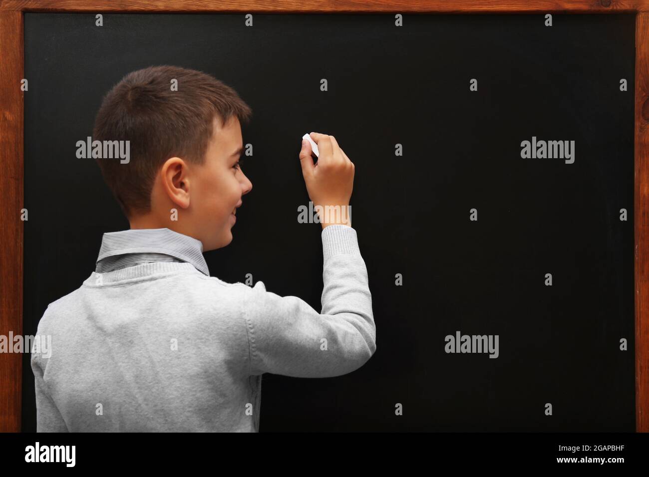 Back view of young schoolboy writing at the blackboard Stock Photo - Alamy