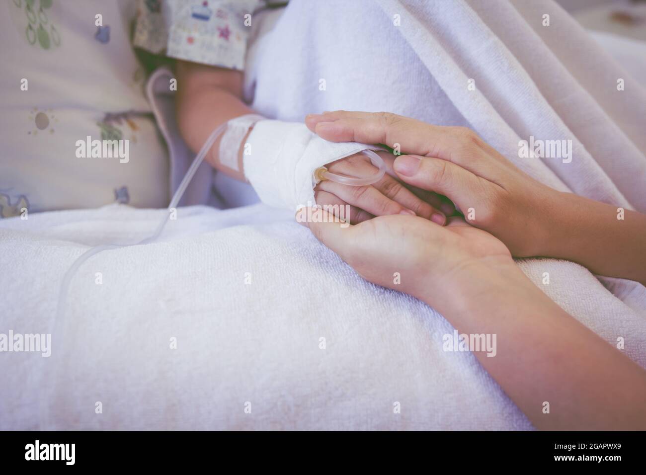 Close up hand of parent holding hand of child in hospital, saline ...
