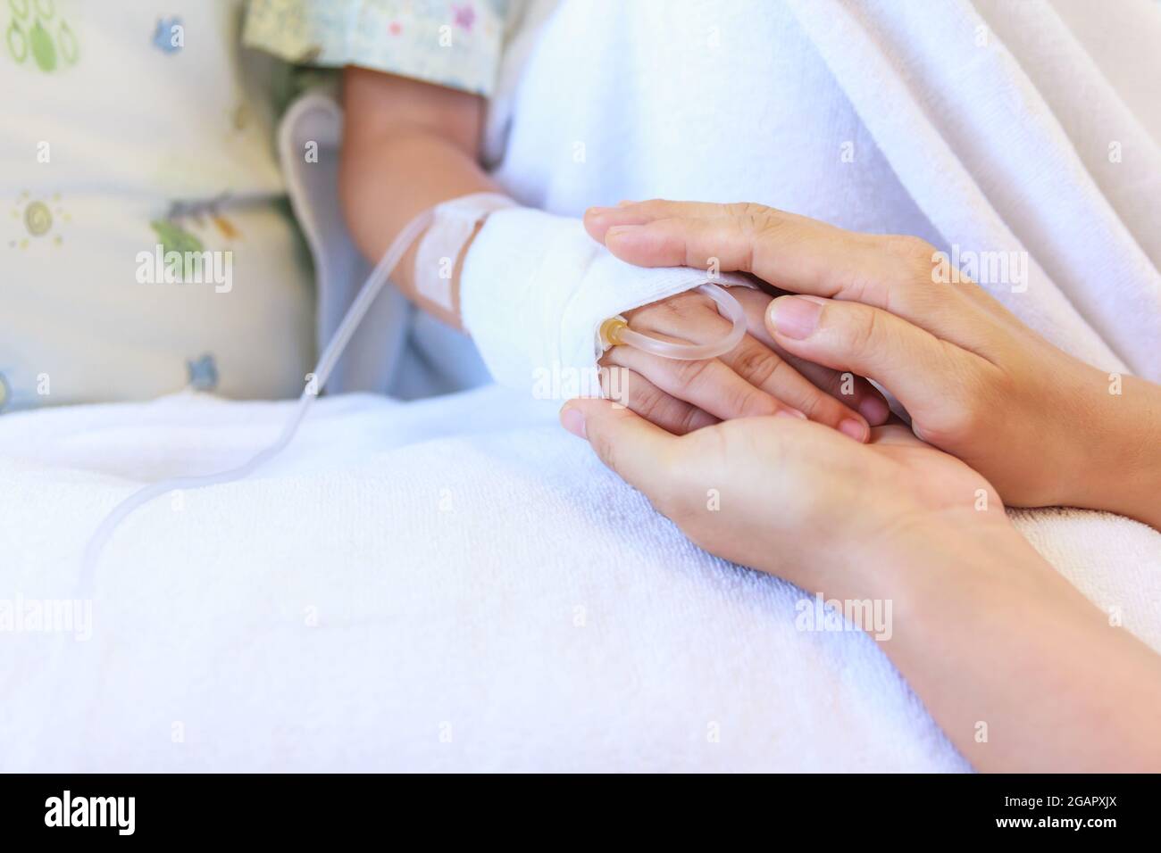 Close up hand of parent holding hand of child in hospital, saline ...