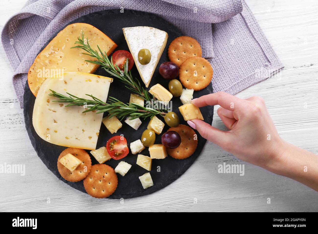 Hand takes peace of cheese from round board with food Stock Photo - Alamy