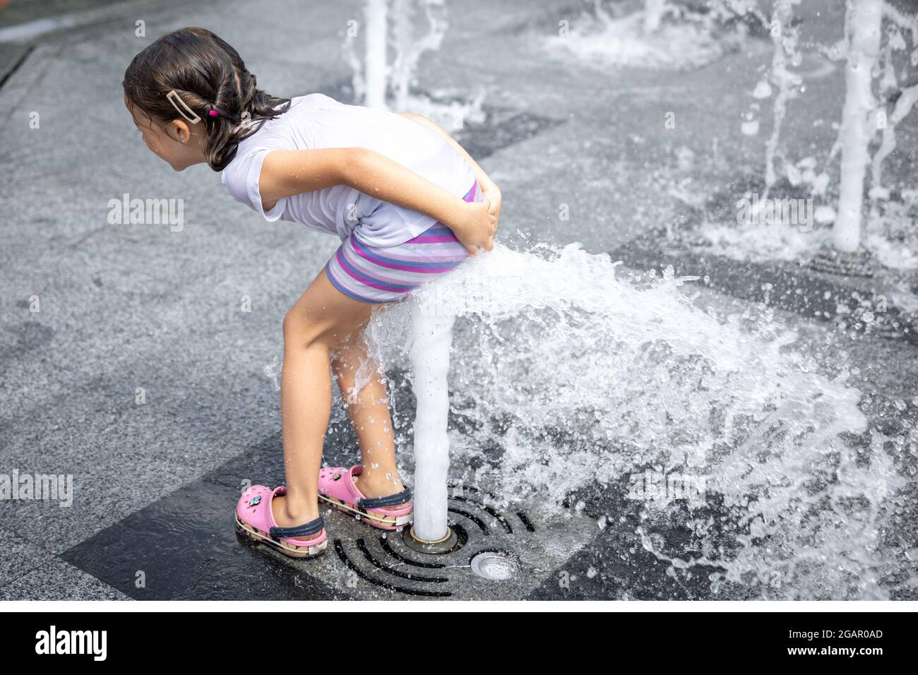 Happy little girl among the splashing water of the city fountain has ...