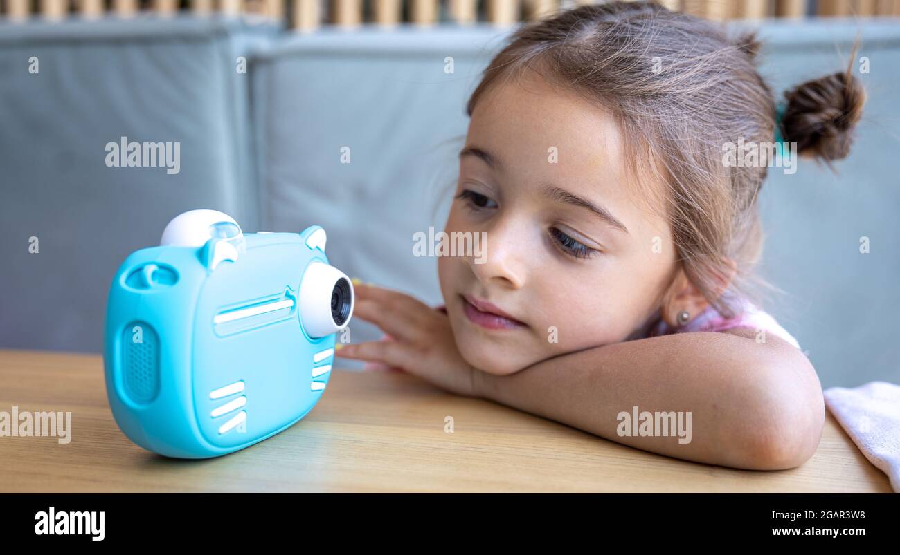 A cute little girl looks at her children's blue toy camera for instant ...