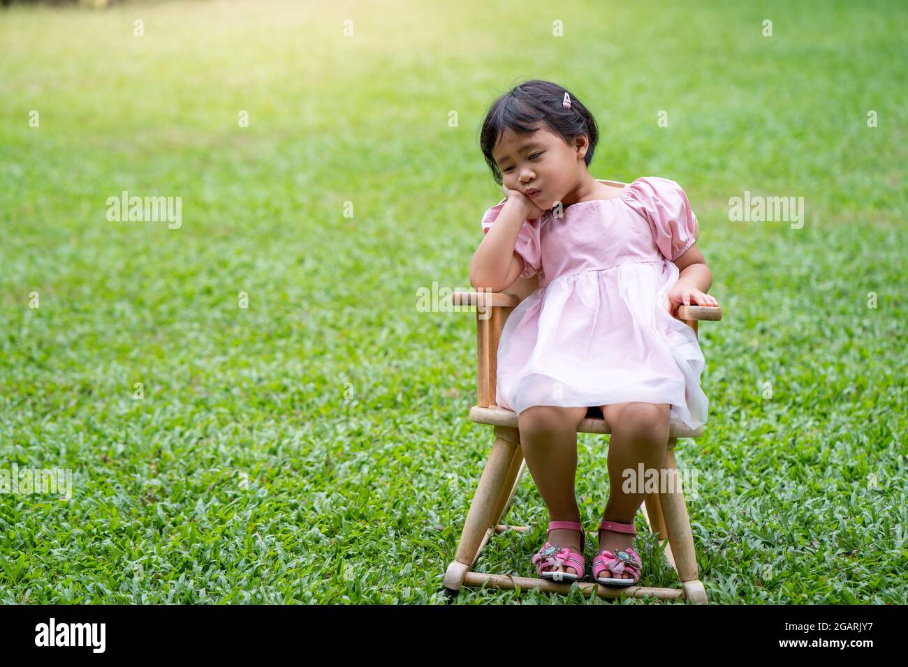 A tired little Asian girl sitting on a chair in the green grass Stock ...