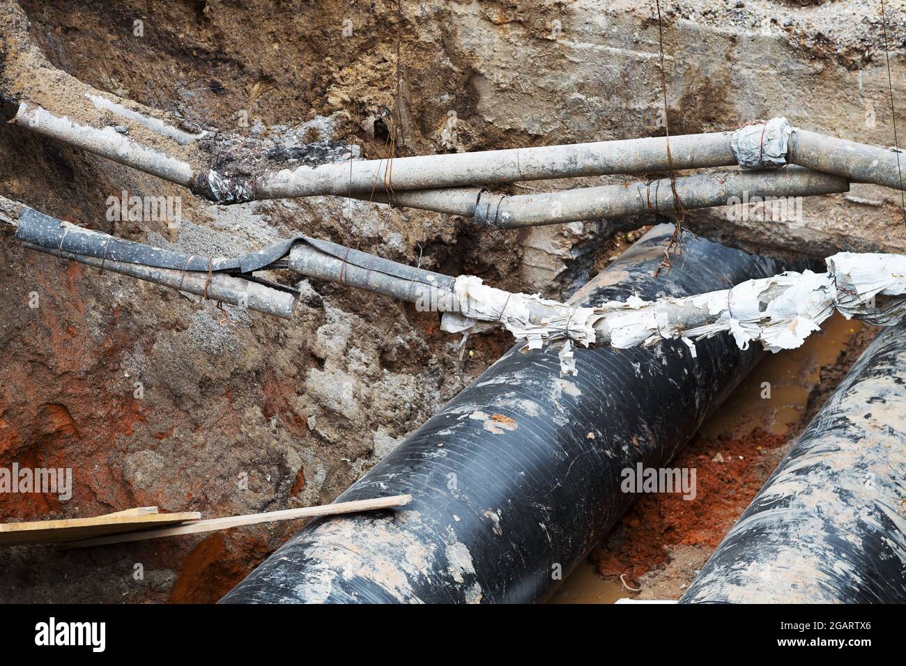 Repair of heating duct. Large iron pipes at a depth of excavated trench ...