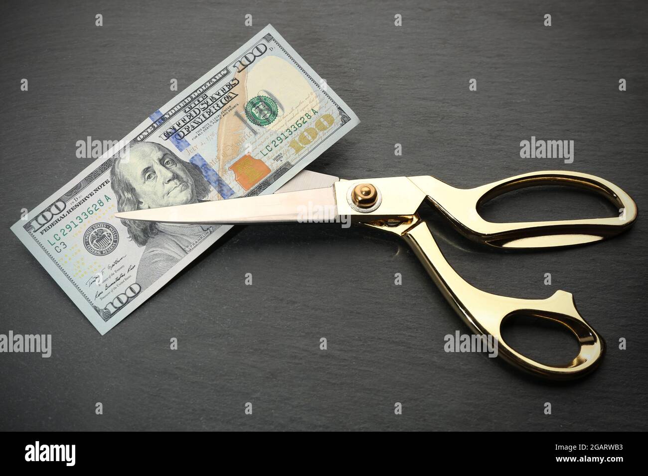 Golden scissors cut money on black background Stock Photo - Alamy