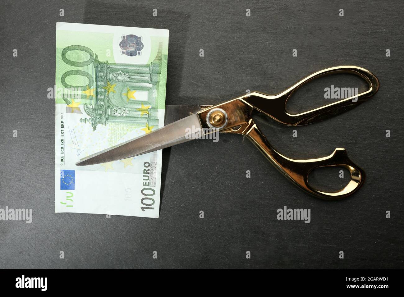 Golden scissors cut money on black background Stock Photo - Alamy
