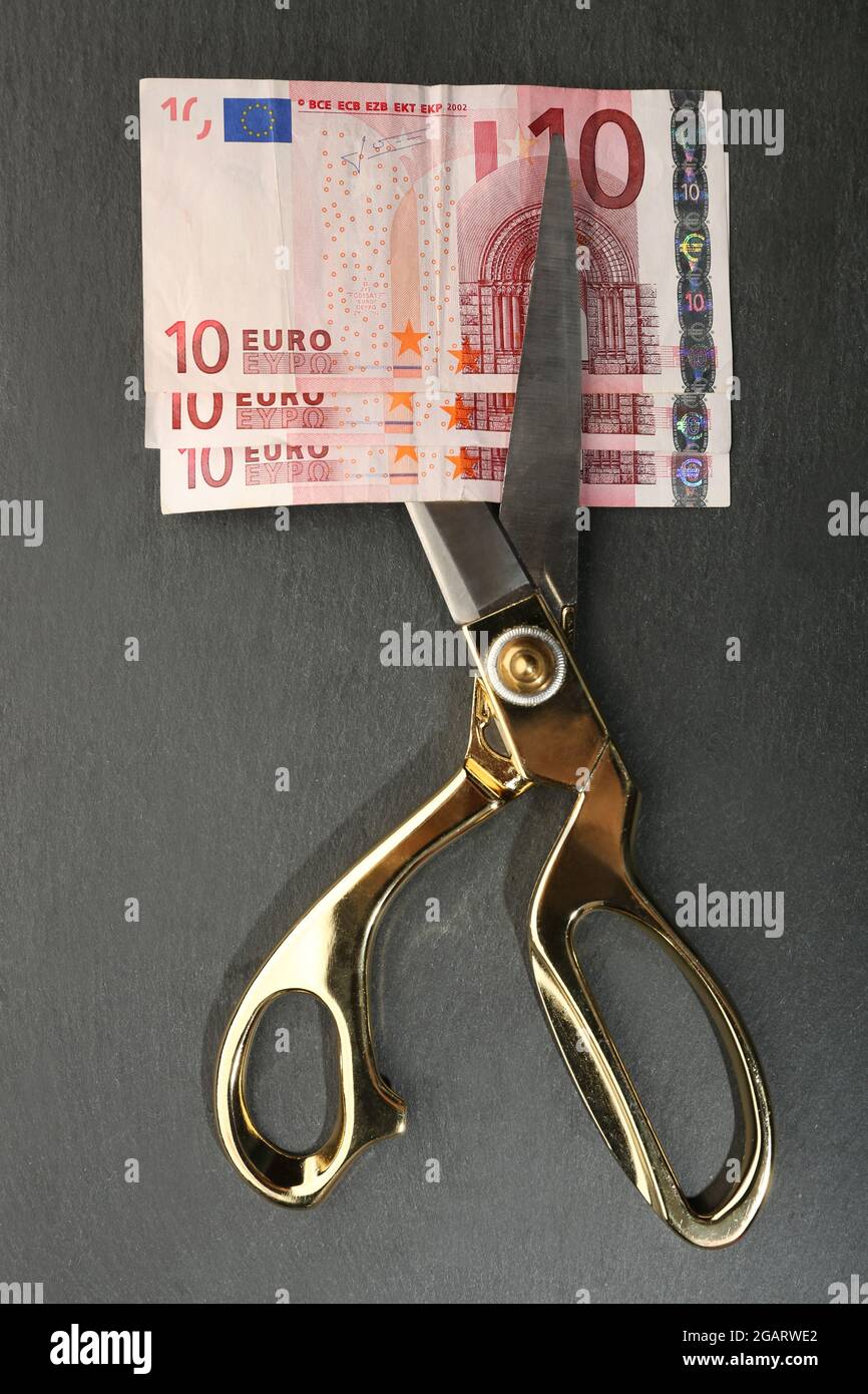 Golden scissors cut money on black background Stock Photo - Alamy