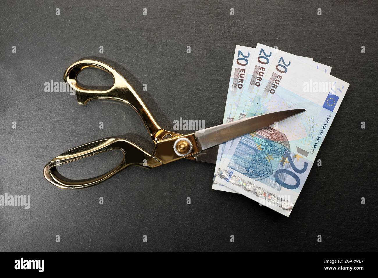 Golden scissors cut money on black background Stock Photo - Alamy