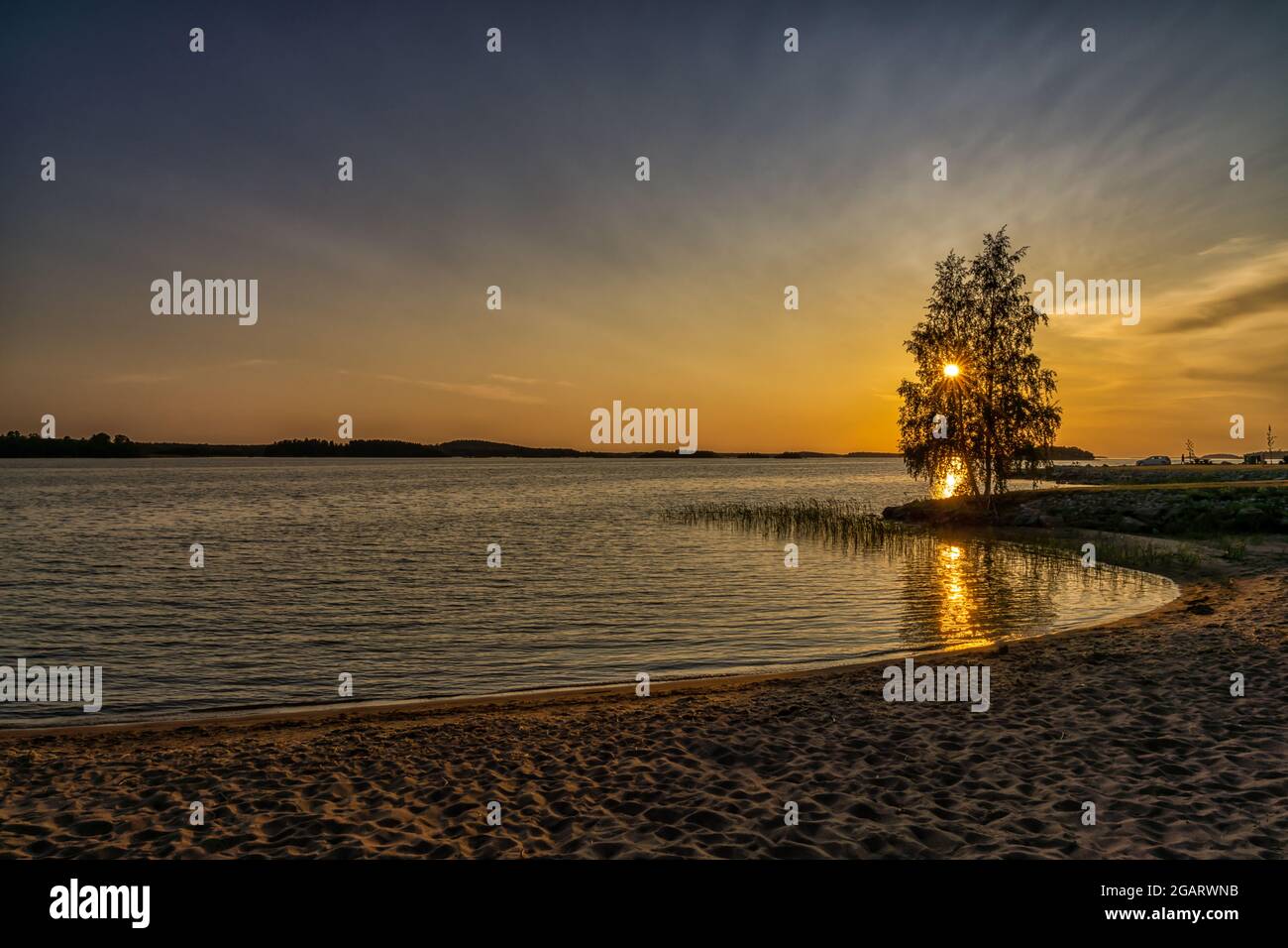 Colorful sunset over a calm ocean with a sandy beach in the foreground ...
