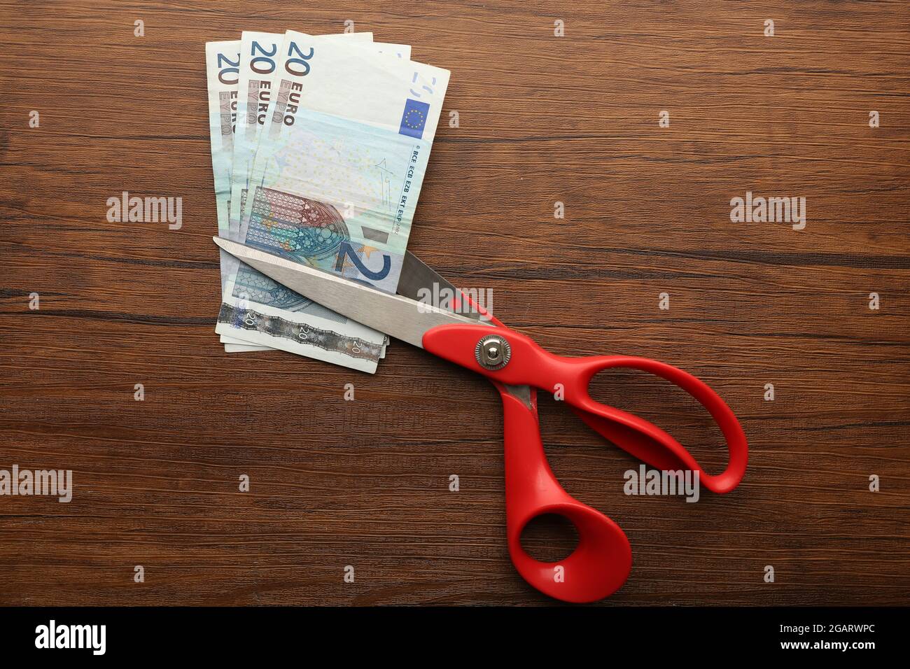Red scissors cut money on wooden background. Financial concept Stock ...