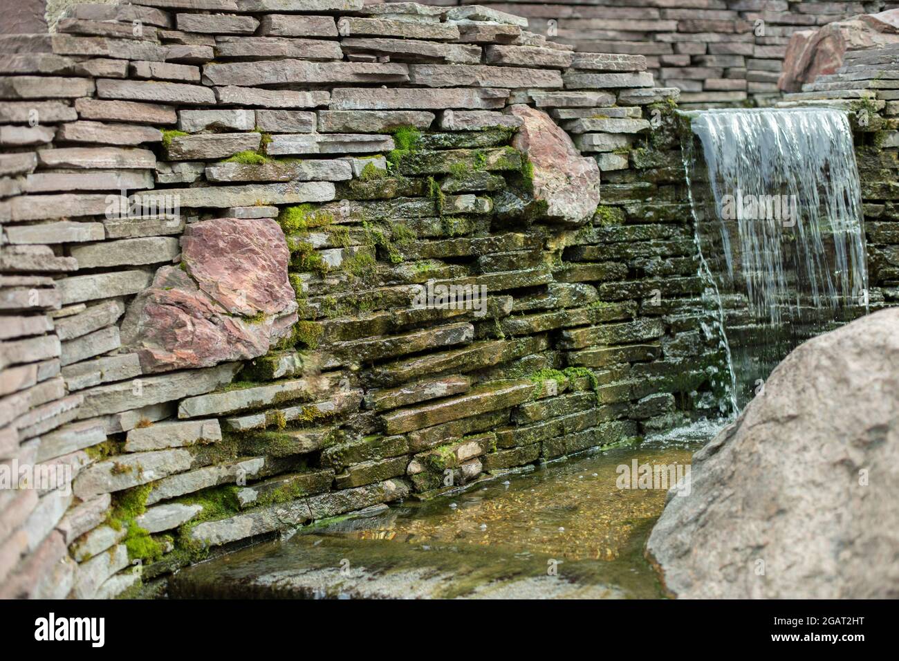 Artificial waterfall. Water runs over the stones. Landscaping in the ...