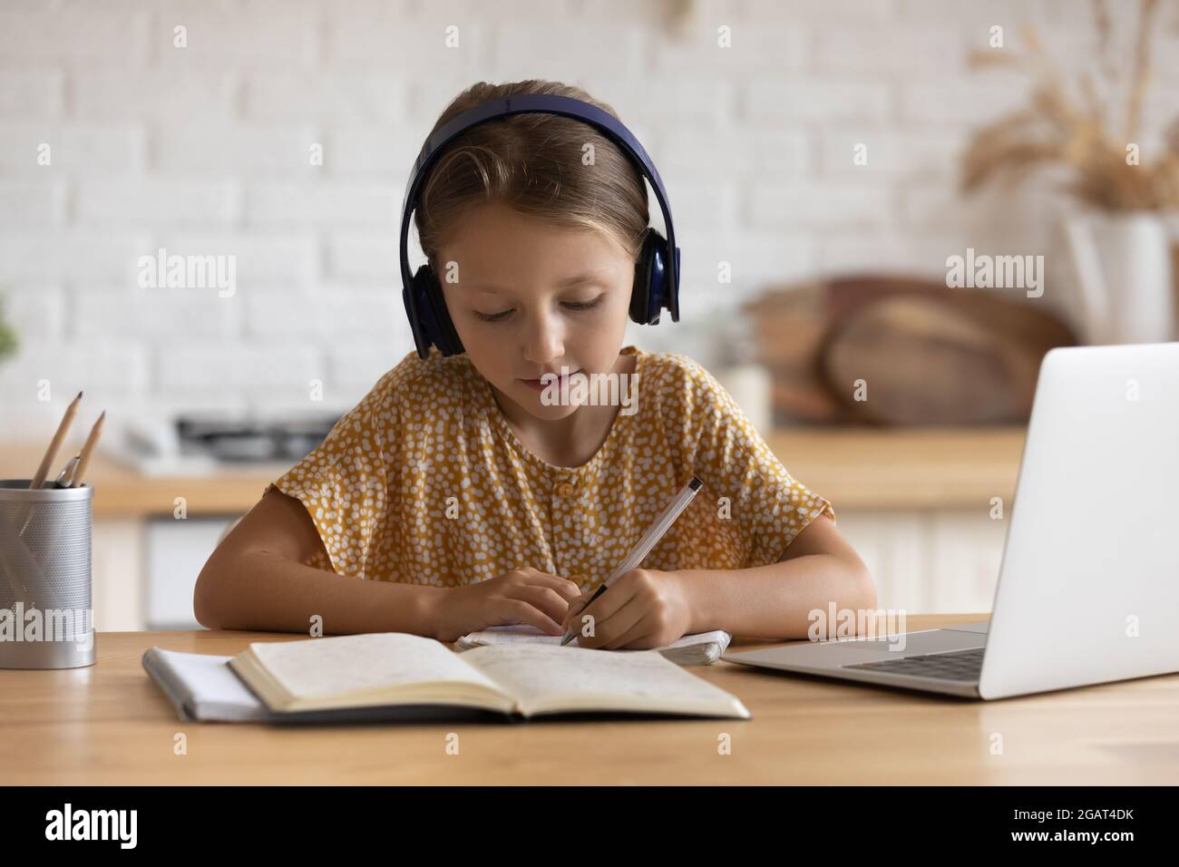 Close up little girl in headphones taking notes studying online Stock ...