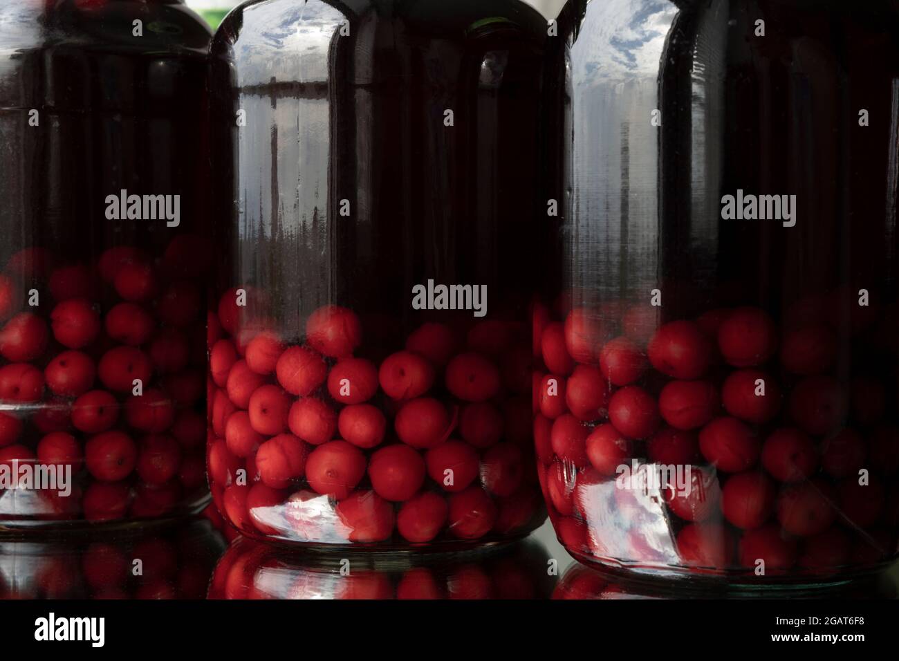 Three glass jars with home-preserved red cherries and their reflections ...